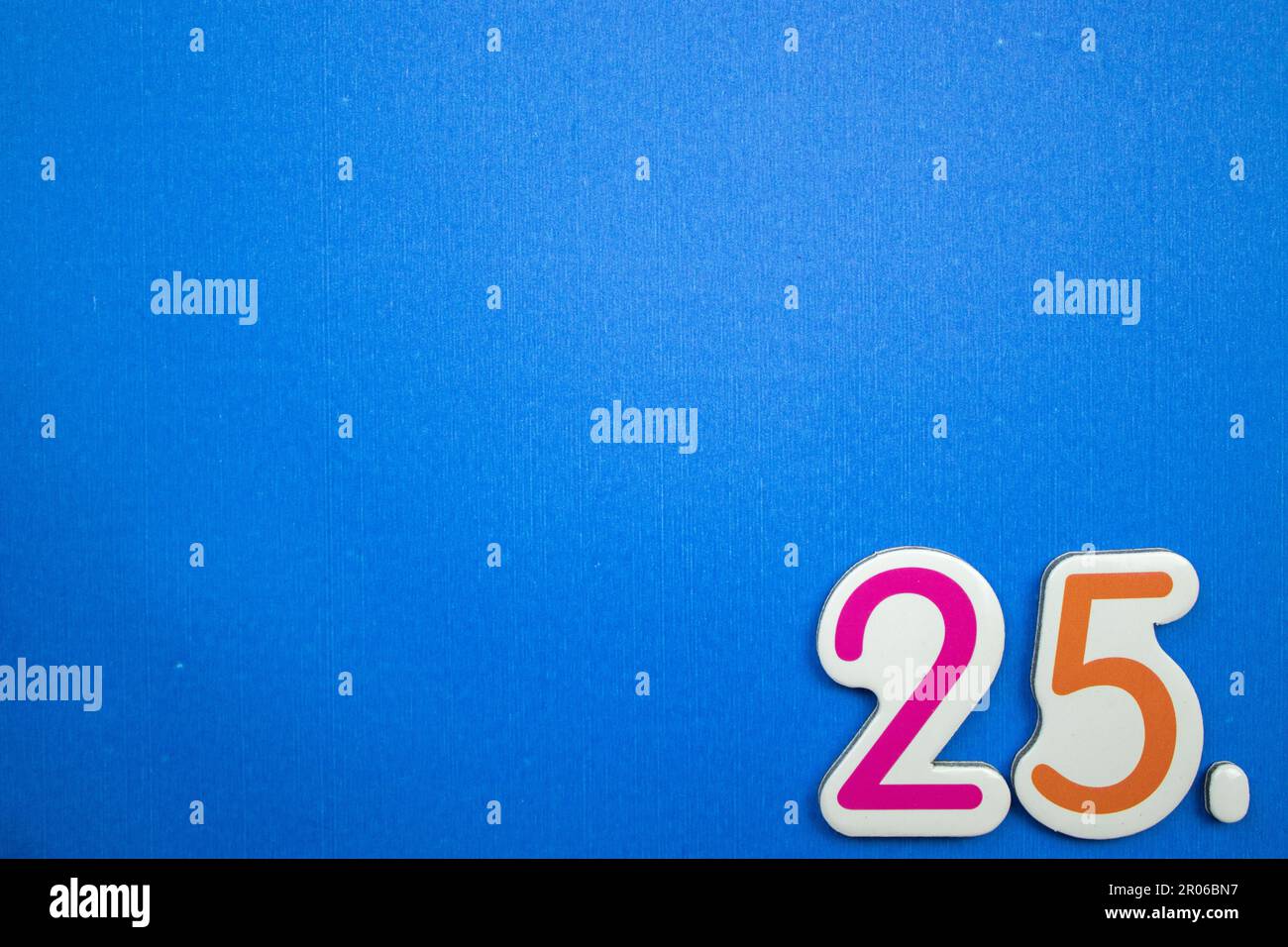 The number 25, placed on the edge of the blue background, photographed from above, colored red ...