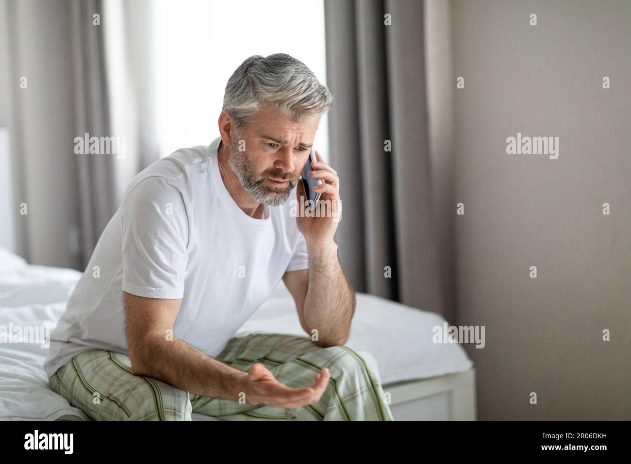 Angry middle aged man sitting on bed, have phone conversation Stock ...