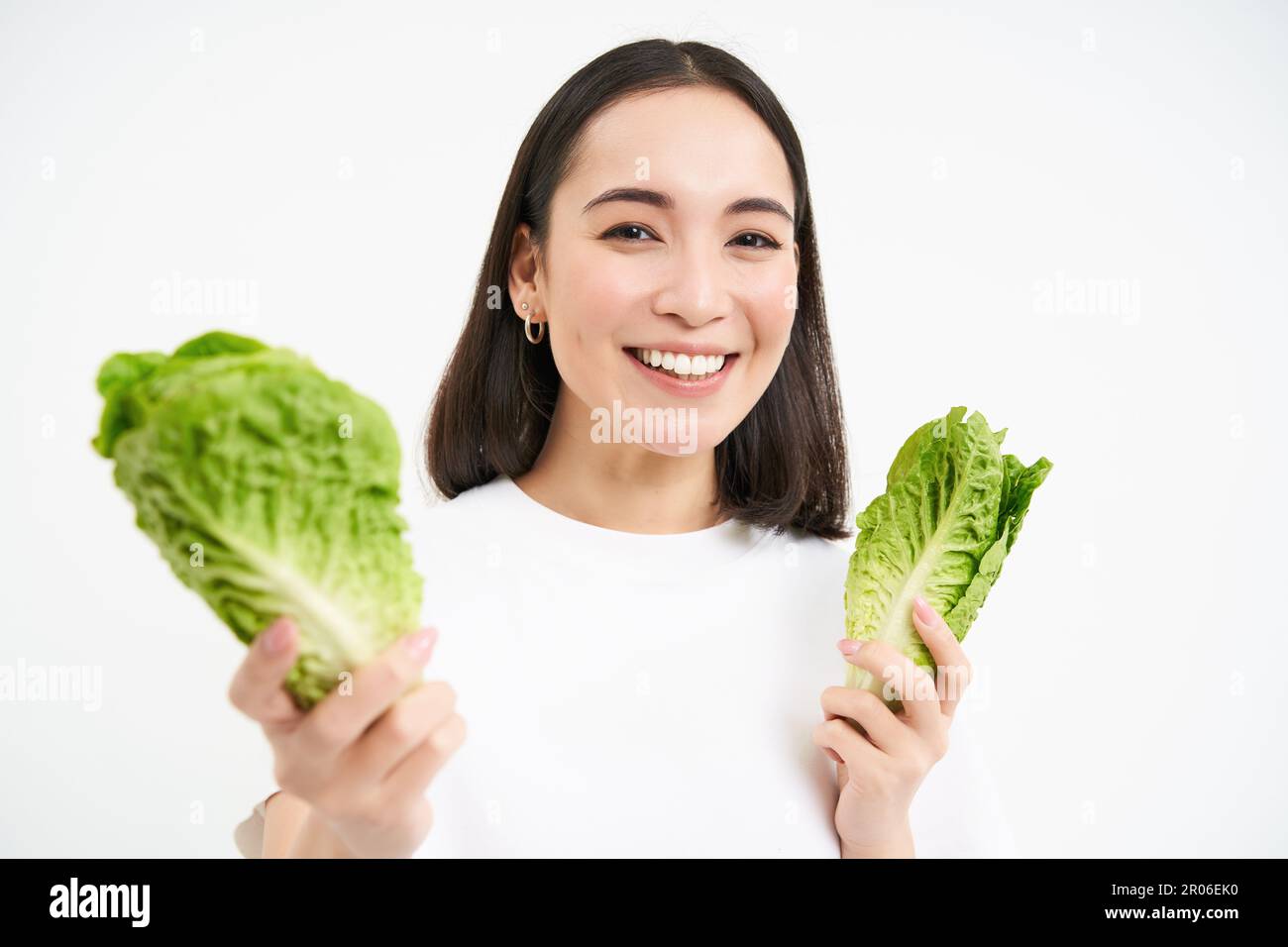 Smiling asian woman, vegan eating cabbage, enjoys tasty fresh lettuce ...