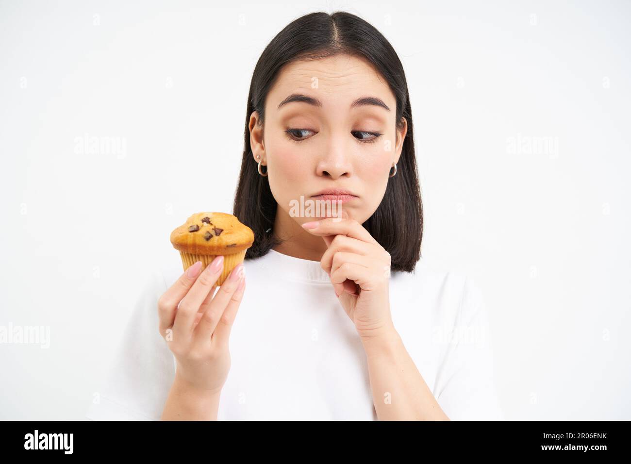 Image of pensive korean woman, looks at cupcake with thoughtful face ...