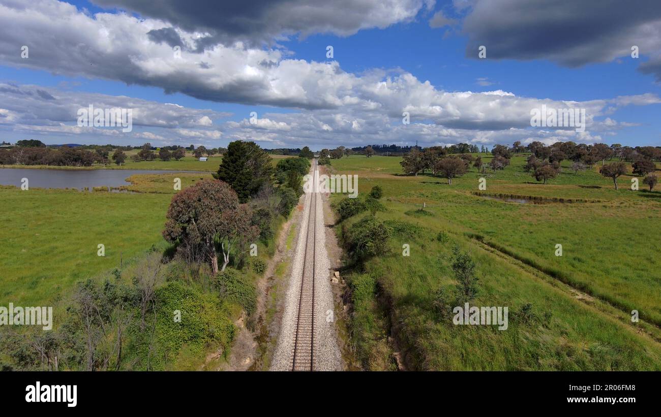 An aerial shot of a train tracks along green meadows and a body of ...