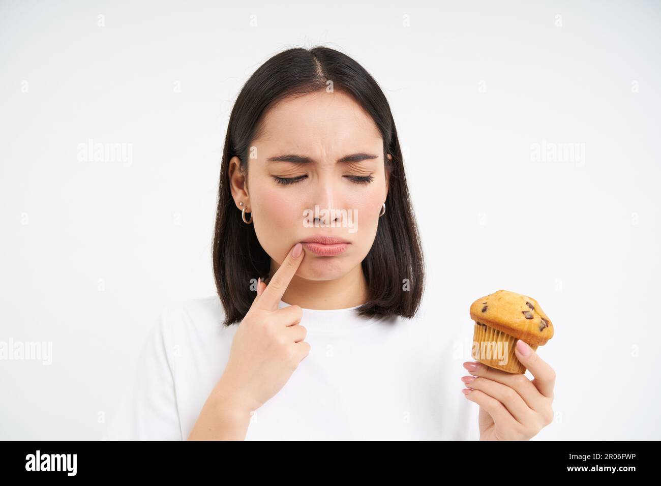 Image of pensive korean woman, looks at cupcake with thoughtful face ...