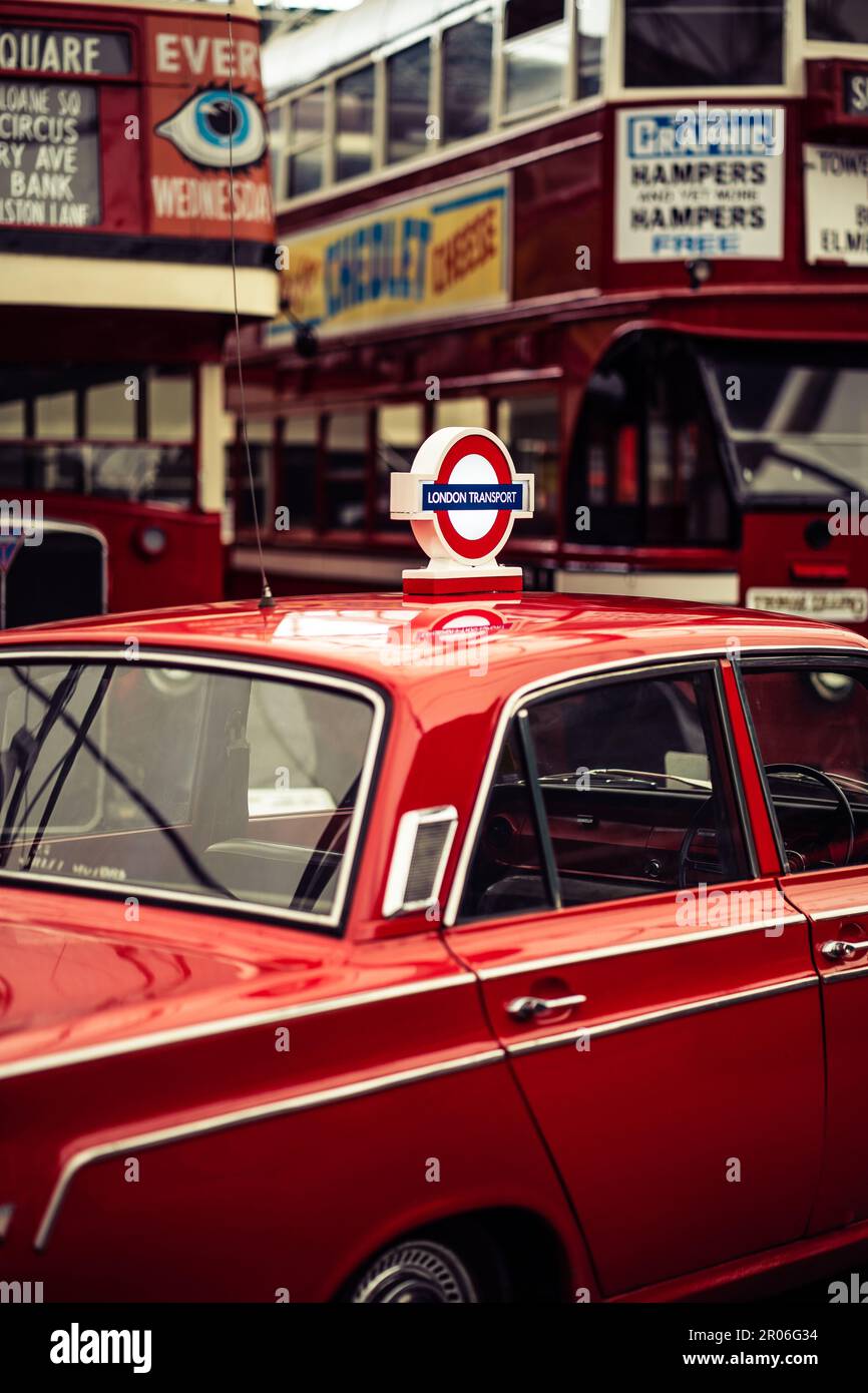 A red vintage car parked alongside a road with "London Transport" sign ...