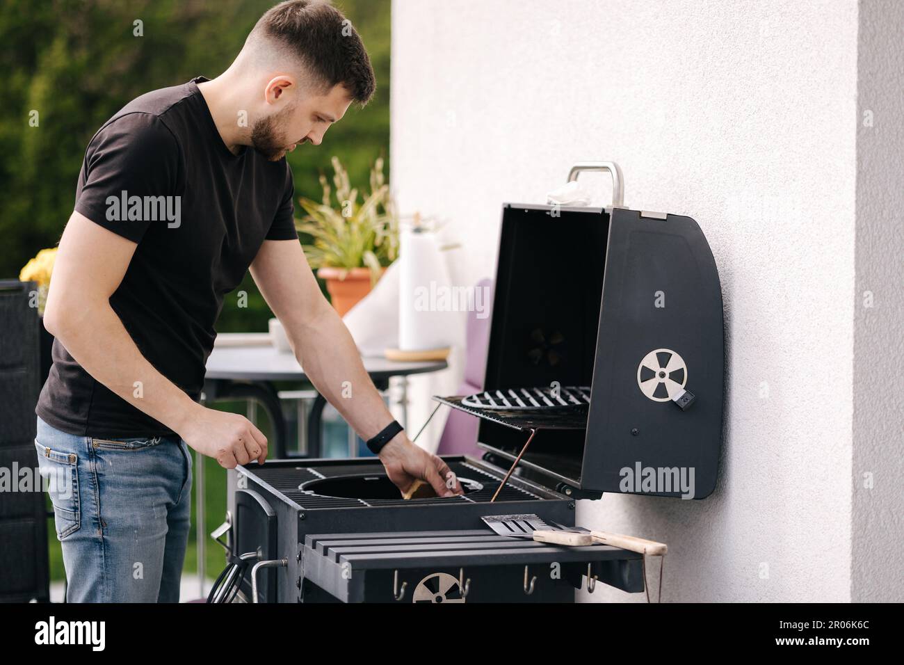 Portrait of handsome young man stand by BBQ grill on terrace. Put hand ...