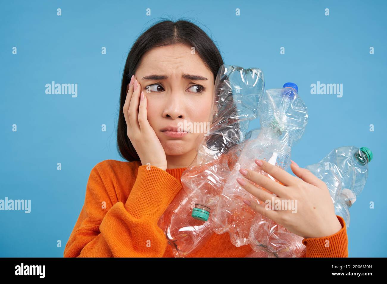 Sad asian woman holding plastic bottles, looking troubled and upset ...