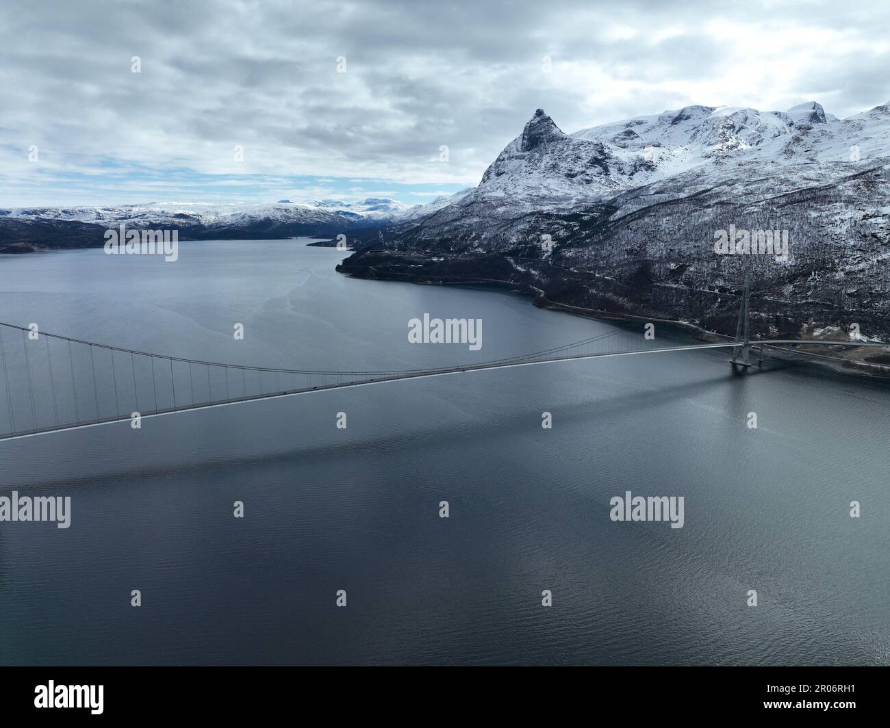 An aerial view of a a suspension bridge over water near snow-capped ...