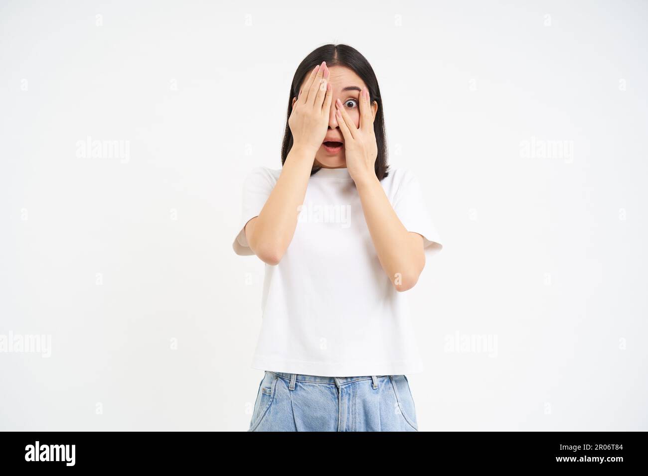 Scared woman shuts her eyes, peeks through fingers with shocked ...