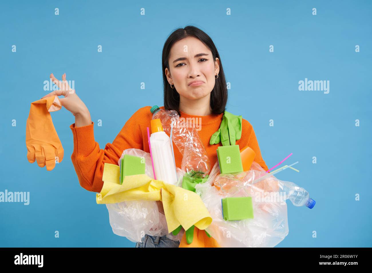 Upset asian girl holds cleaning items, plastic waste, looks sad and ...