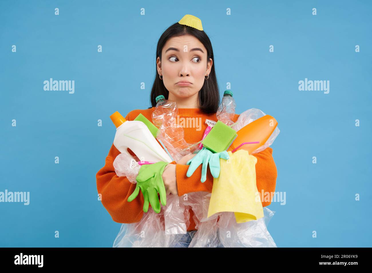 Confused young asian woman, holding plastic bottles, household garbage ...