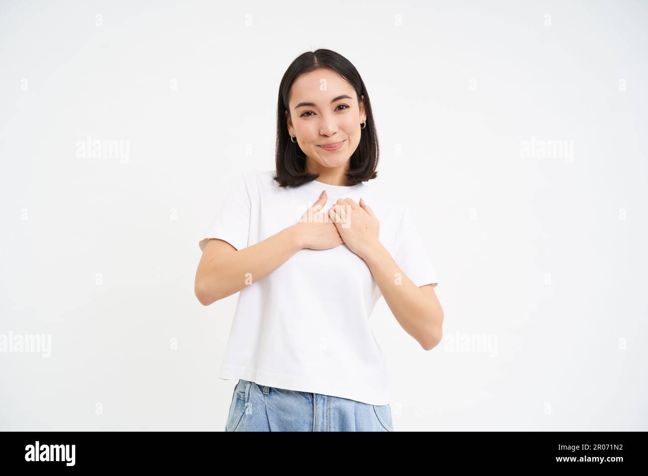 Smiling young korean woman, holds hands on heart, concept of love ...