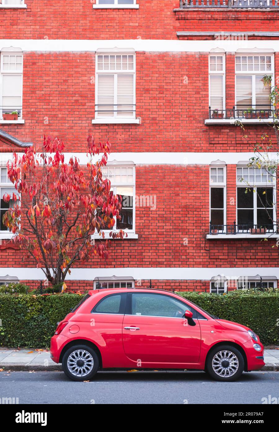 Vertical photo of a red small car parked in front of a red brick ...
