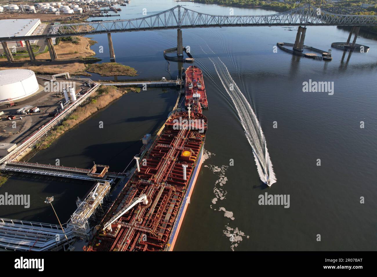 A boat passes under the Outerbridge Crossing and past chemical tankers ...