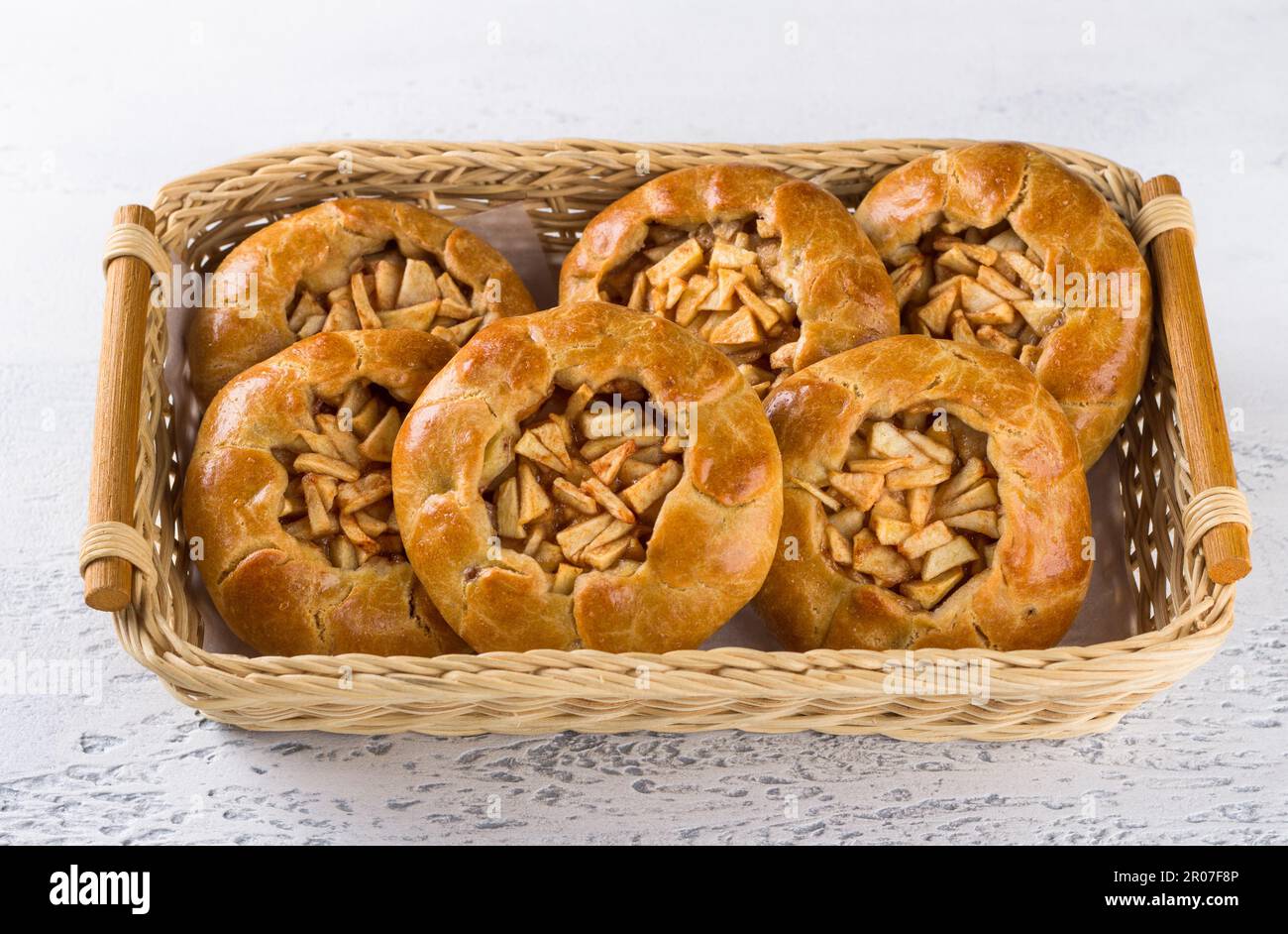 Sweet mini pies with apples and cinnamon in a wicker basket on a light ...