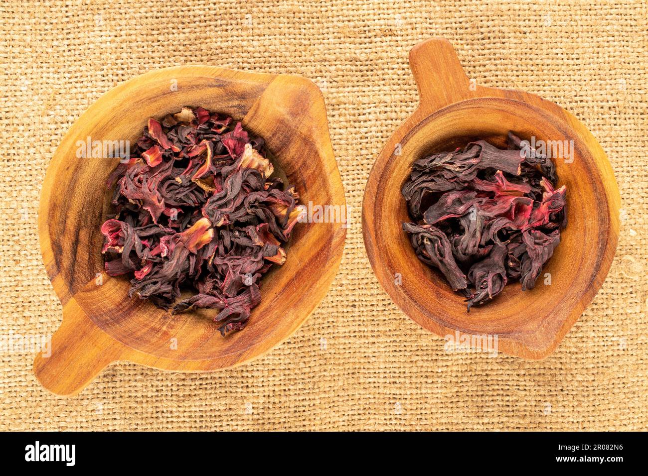 Dry fragrant karkade tea in two wooden cups on a jute cloth, macro, top ...