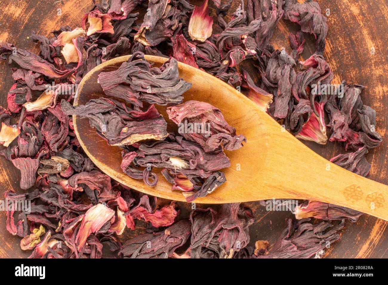 Dry fragrant karkade tea with a wooden spoon on a clay dish, macro, top ...