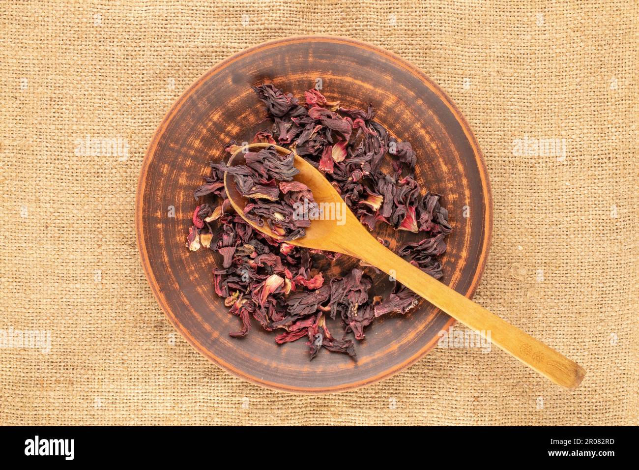 Dry fragrant karkade tea with clay plate and wooden spoon on jute cloth ...