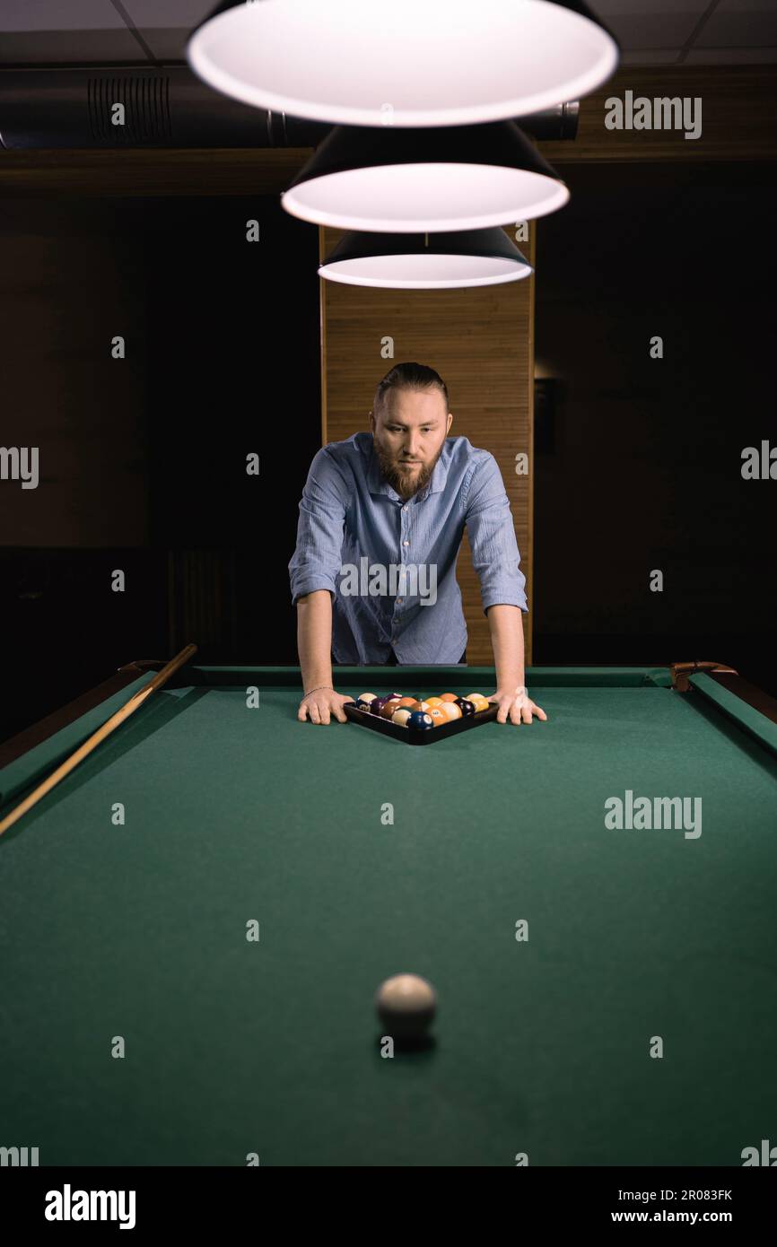 American billiard poule. Handsome man making triangle of billiard balls ...