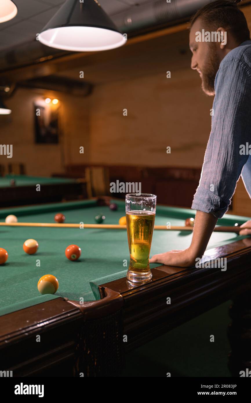 Serious man standing near pool table with fresh beer. A glass of cold ...