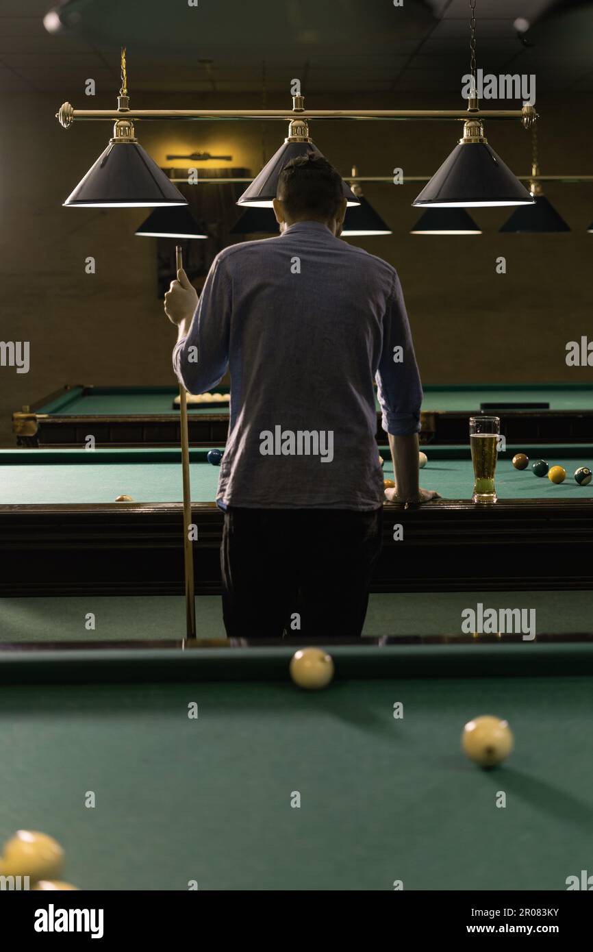 Concentrated young man playing billiards in a club standing between ...