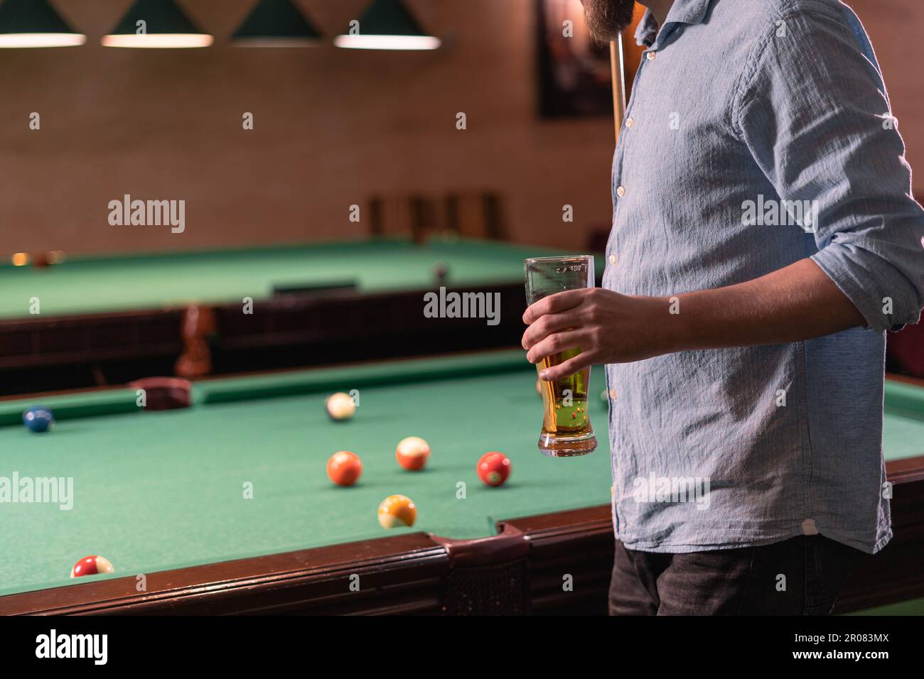 Unrecognizable man with a glass of beer standing near the pool table ...