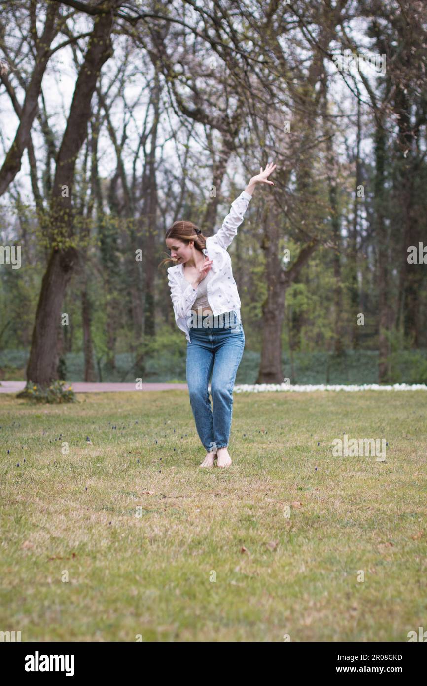 Young woman dancing in the park, in the middle of an elegant jump move ...