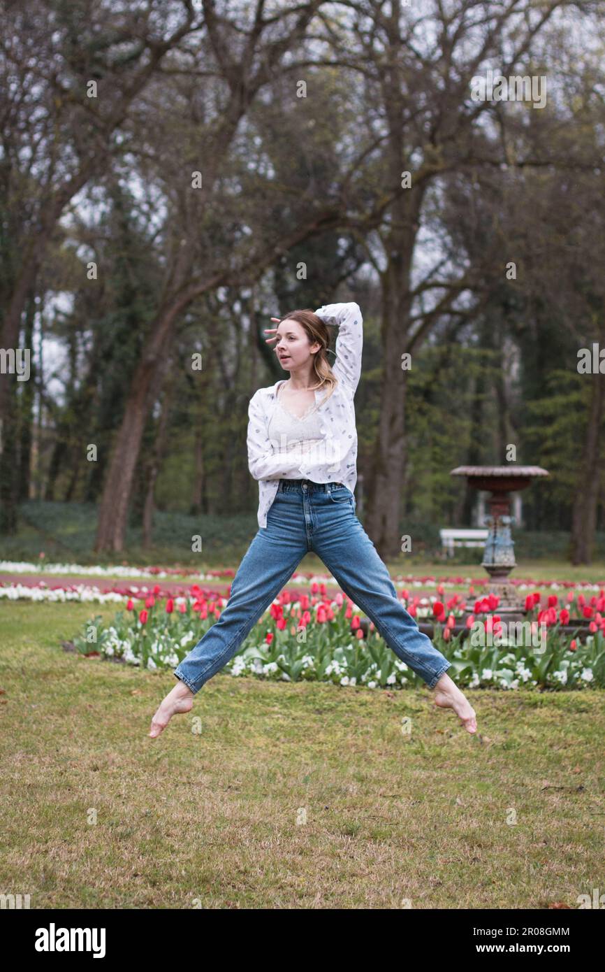 Young woman dancing in the park, in the middle of an elegant jump move ...