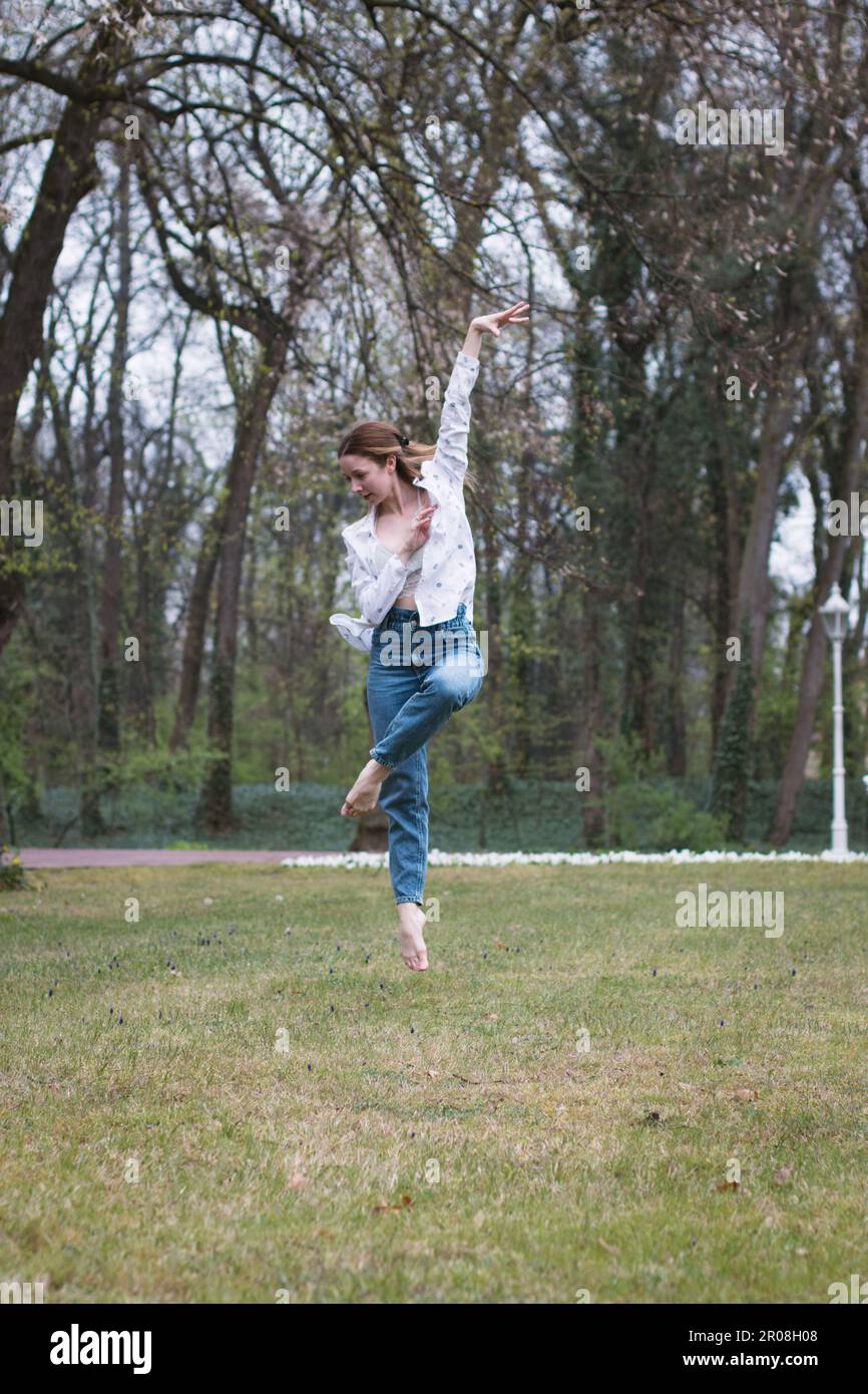 Young woman dancing in the park, in the middle of an elegant jump move ...
