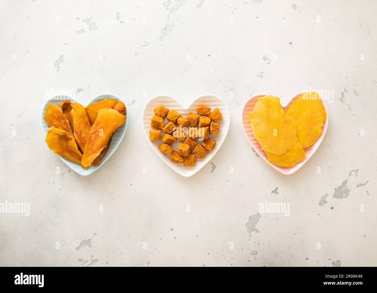 Dried mango slices and balls in heart shaped plates on light background ...