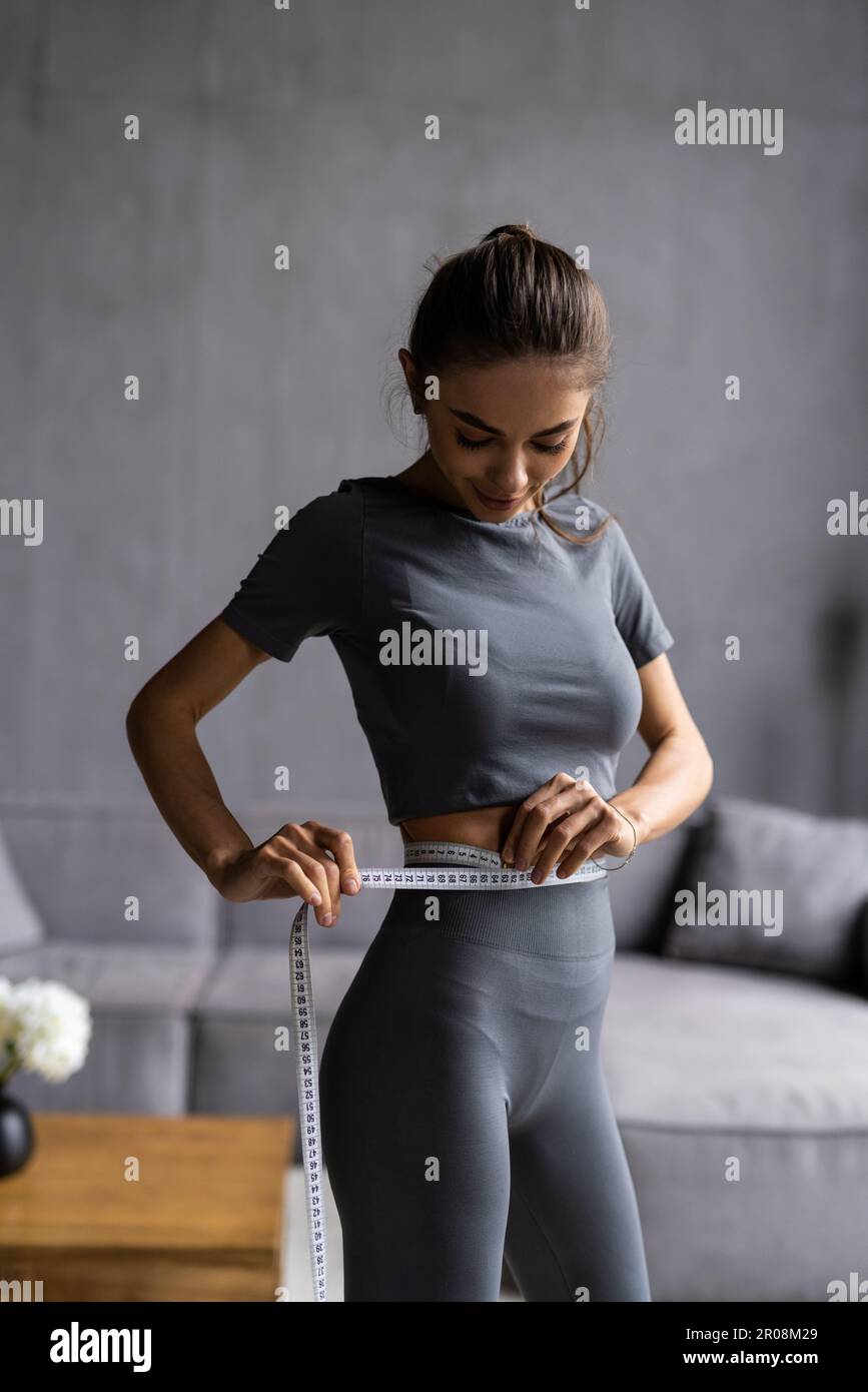 Portrait of young woman measuring her body with tape measure at home ...