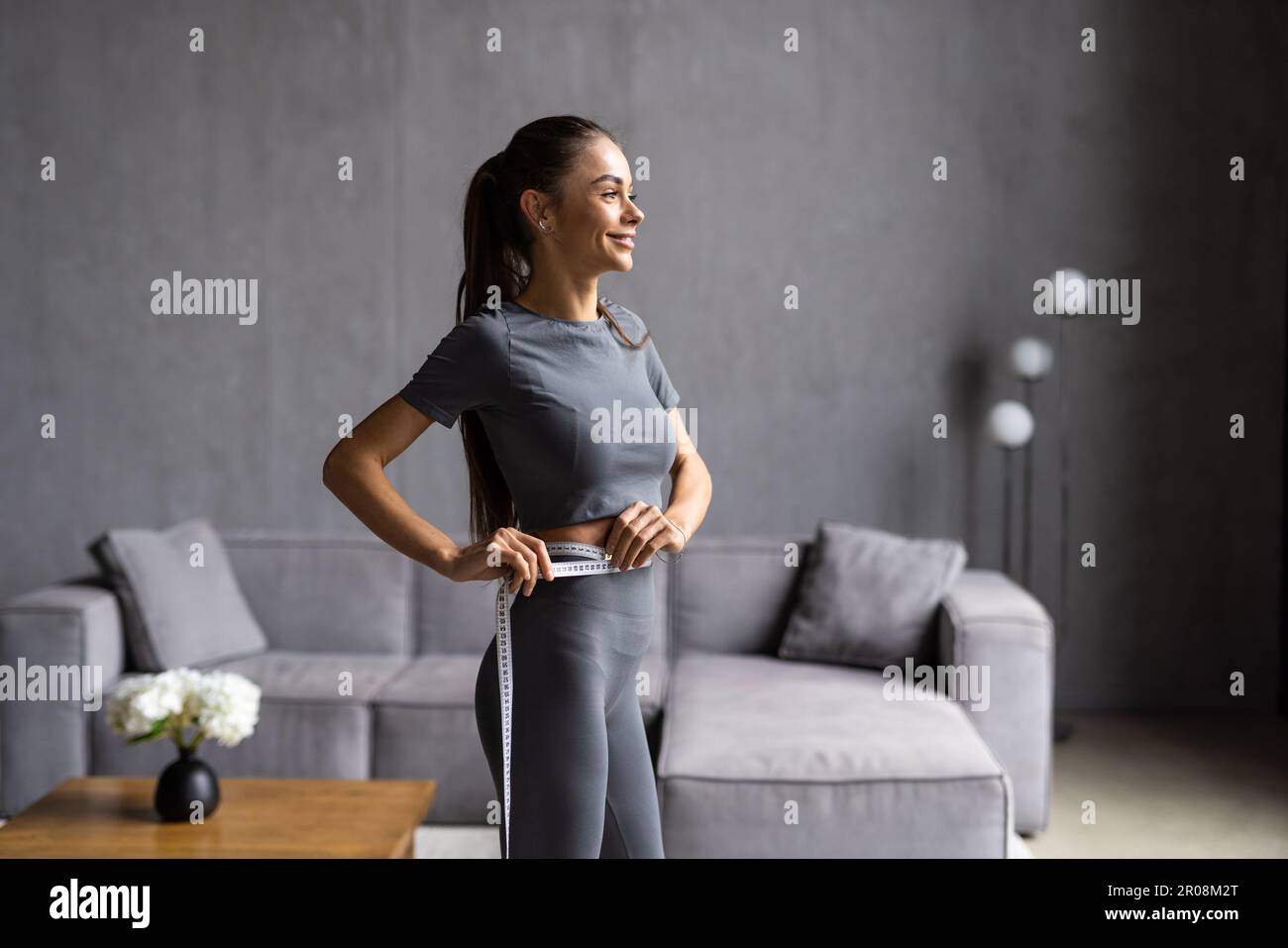 Portrait of young woman measuring her body with tape measure at home ...