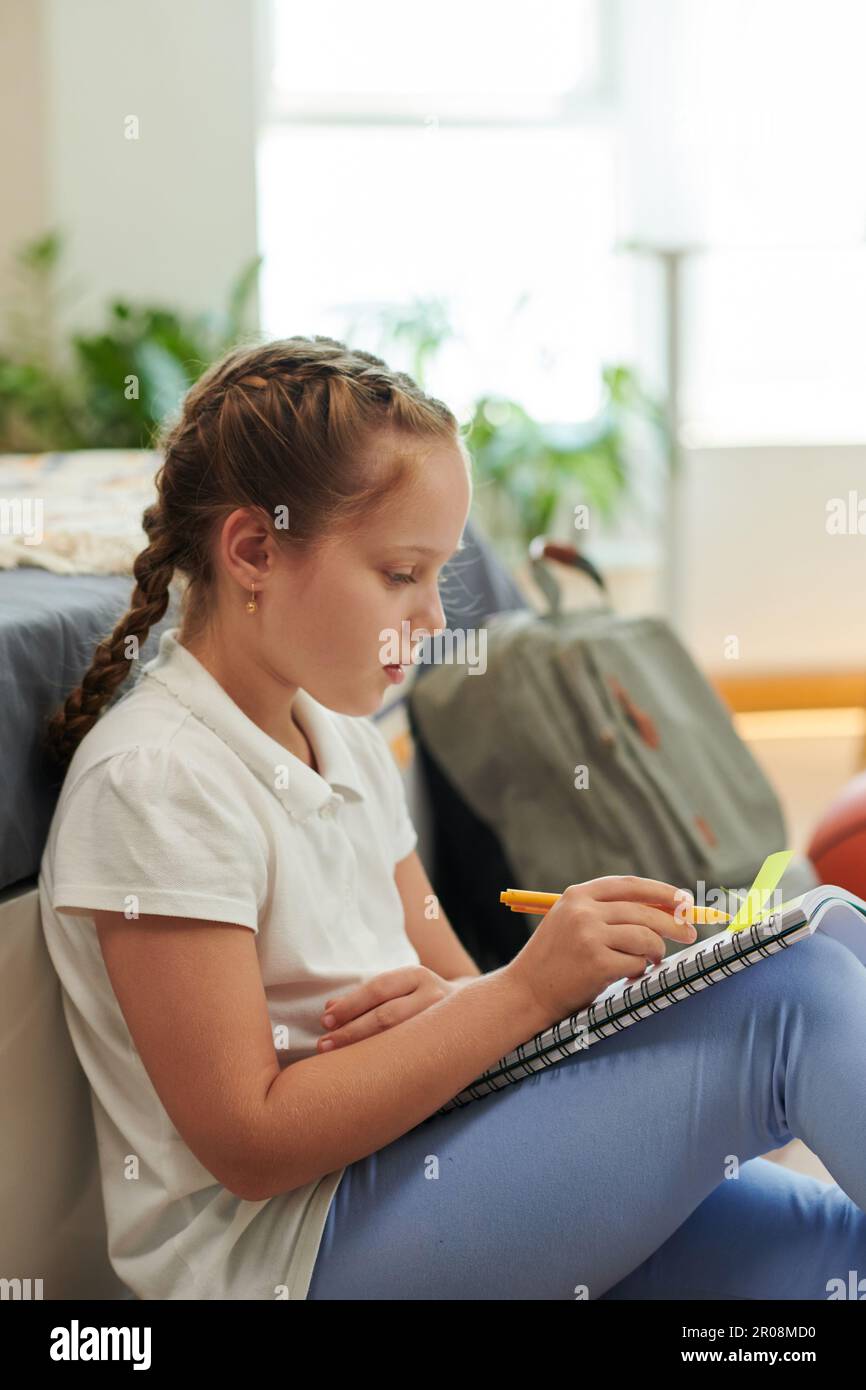 Smart girl working on homework assignment when sitting on floor next to ...