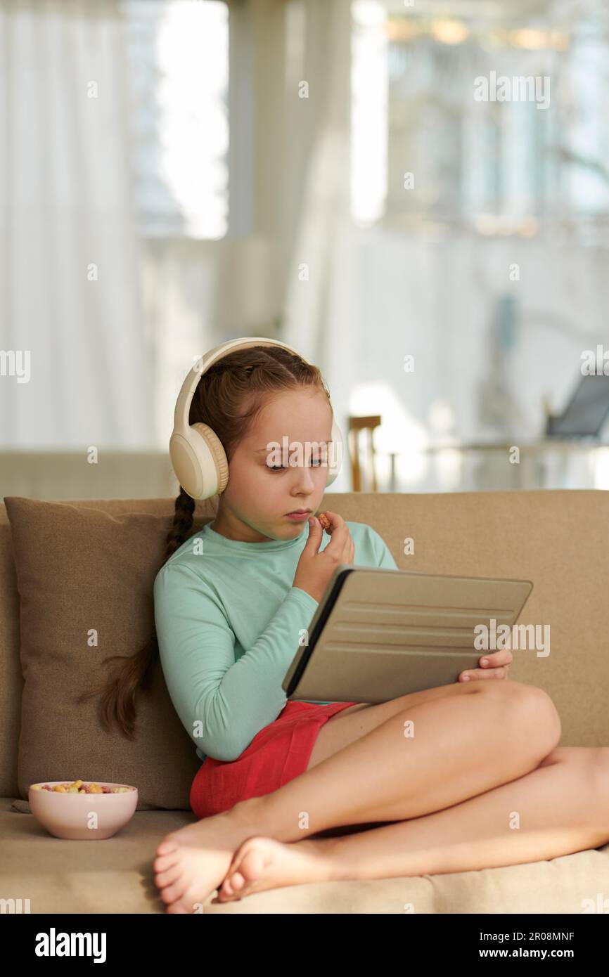 Preteen girl eating snacks when watching her favorite show on tablet ...