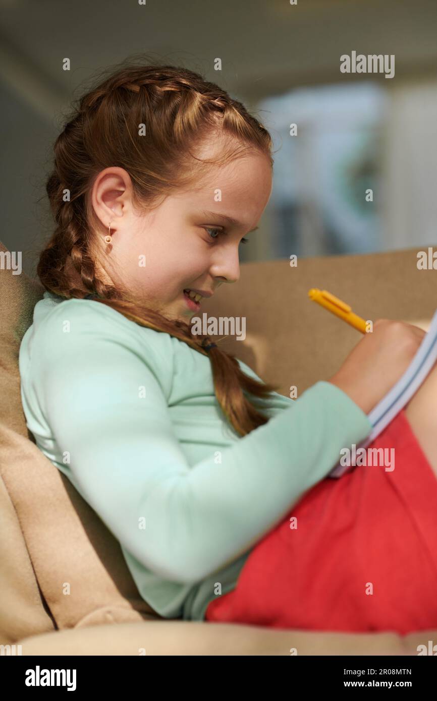 Joyful girl sitting on couch at home and drawing in notepad Stock Photo ...