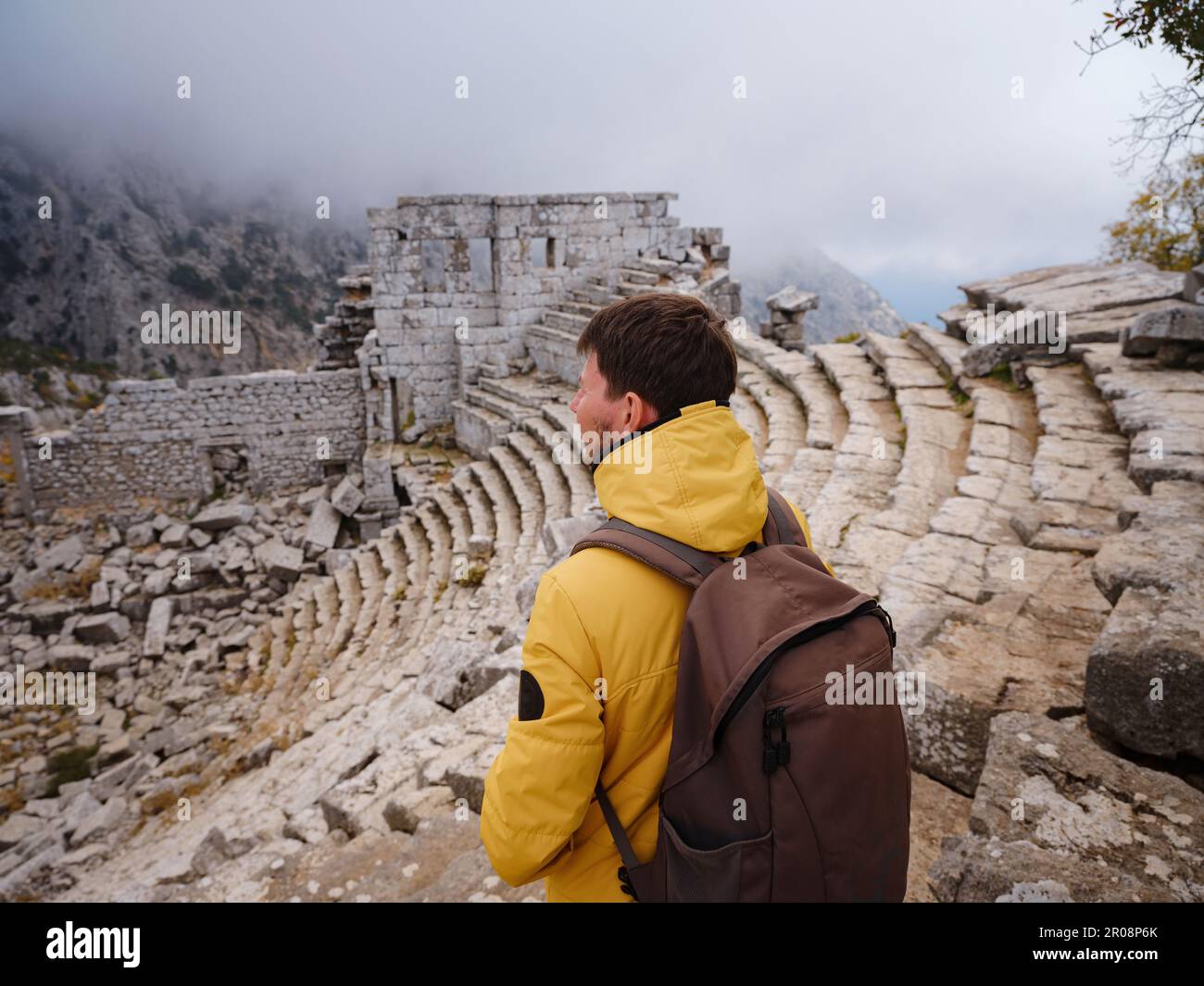 Autumn walk , man in yellow jacket looks at the ancient amphitheatre in ...