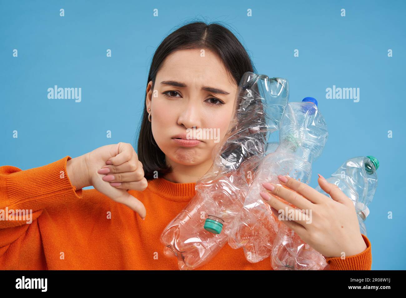 Portrait of woman with upset face, shows thumb down and plastic bottles ...