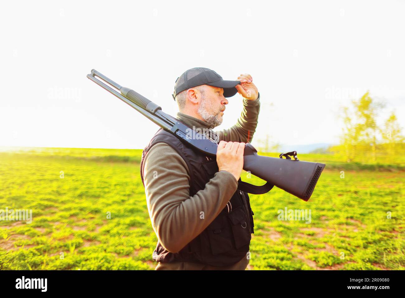 Hunter with a hunting gun on shoulder in the field holding a cap. Rifle ...
