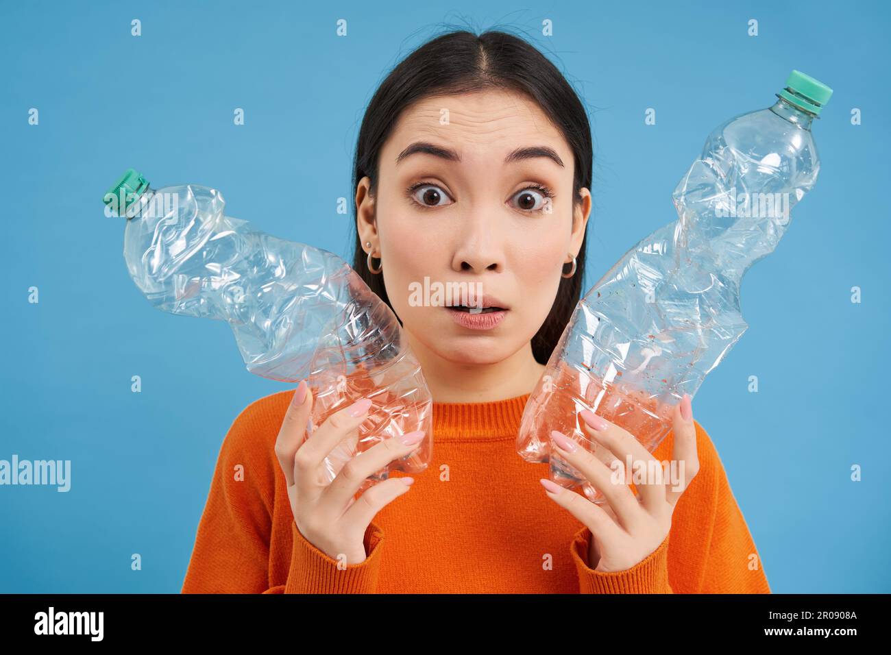Portrait of girl with two plastic bottles, looks confused, tried to ...
