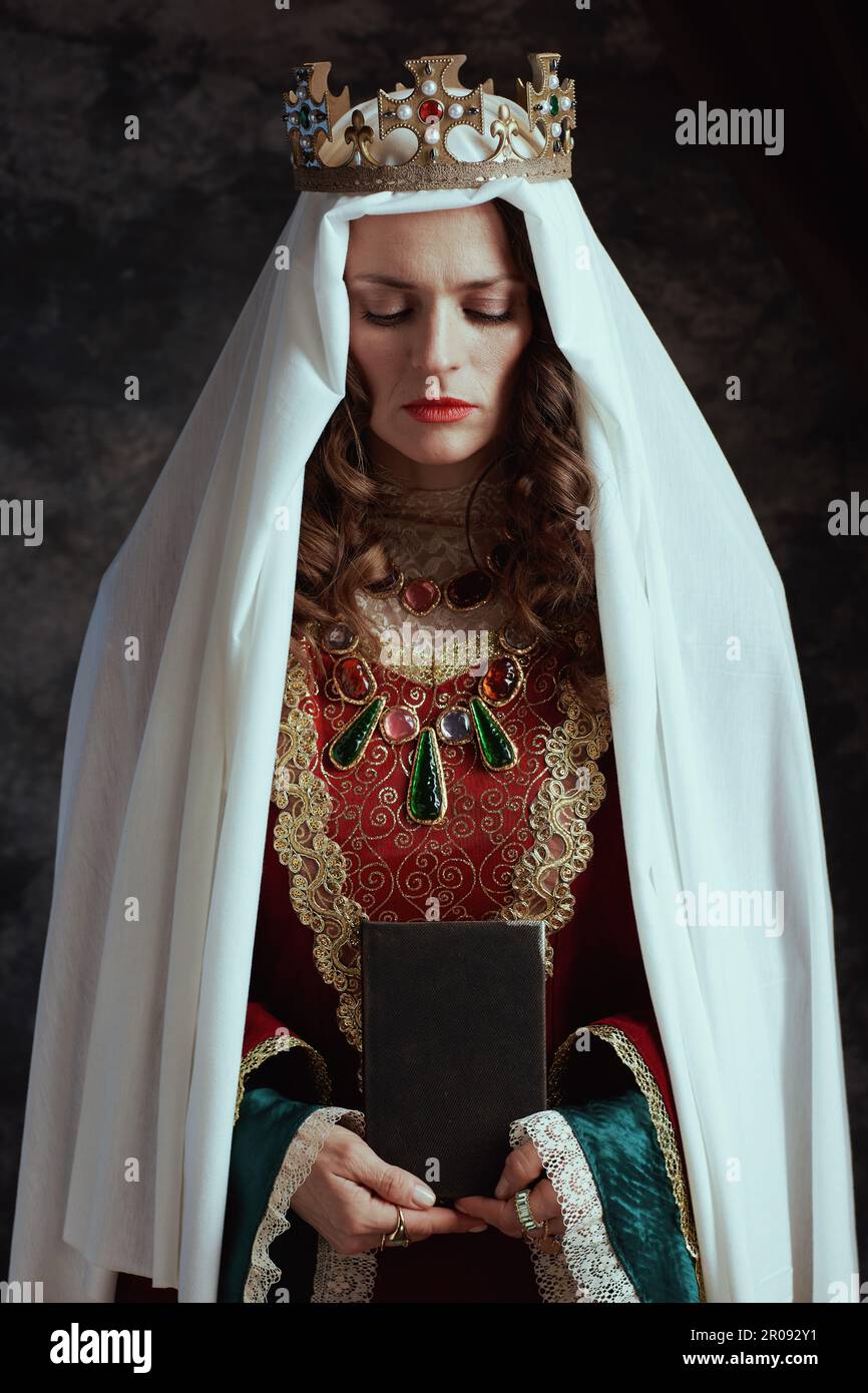 medieval queen in red dress with book, veil and crown on dark gray ...