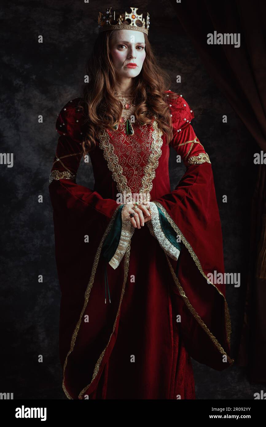 medieval queen in red dress with white makeup and crown on dark gray ...