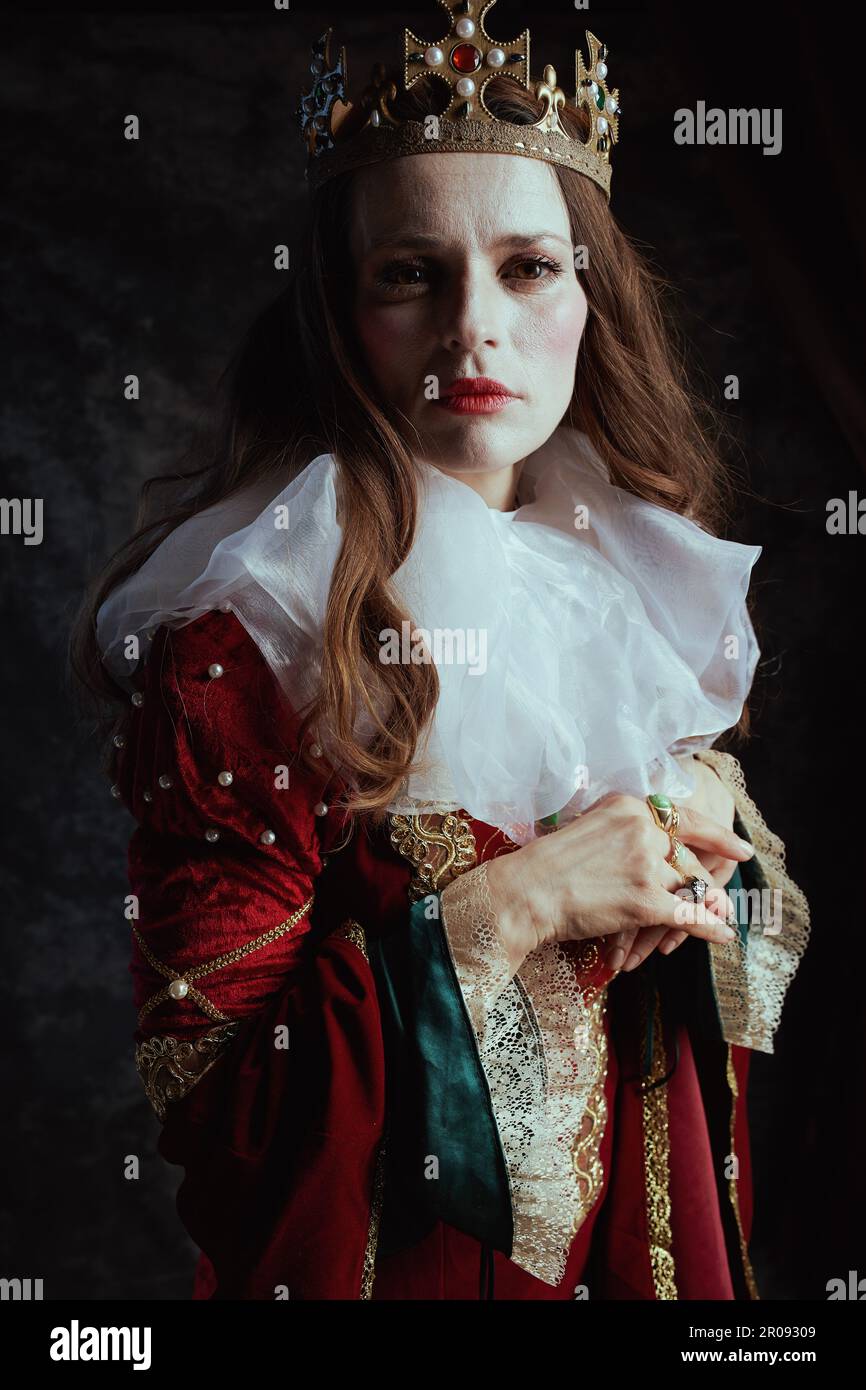 scary medieval queen in red dress with white collar and crown on dark ...