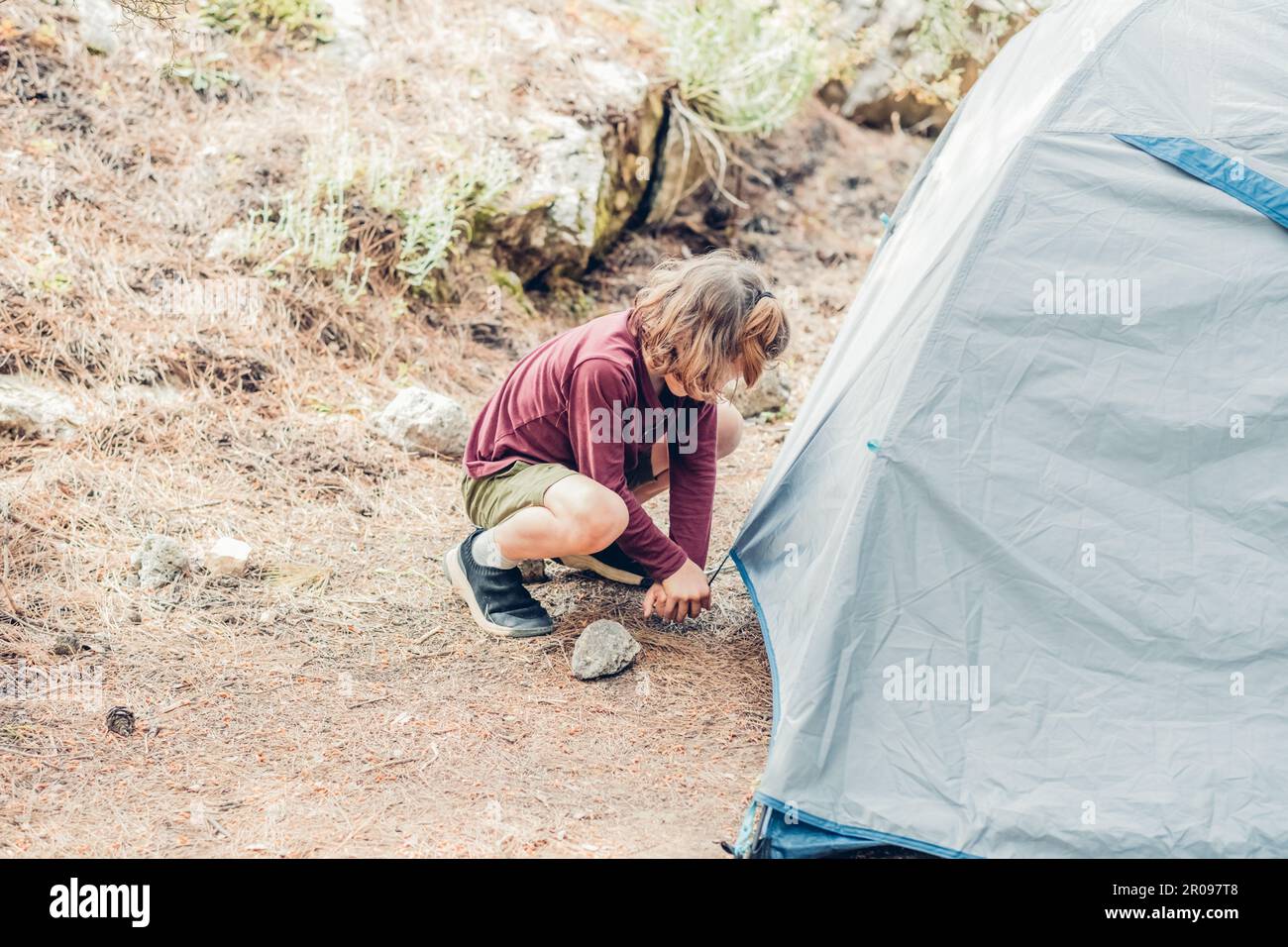Cute boy setting up tourist tent. Summer travel, camping and hiking ...