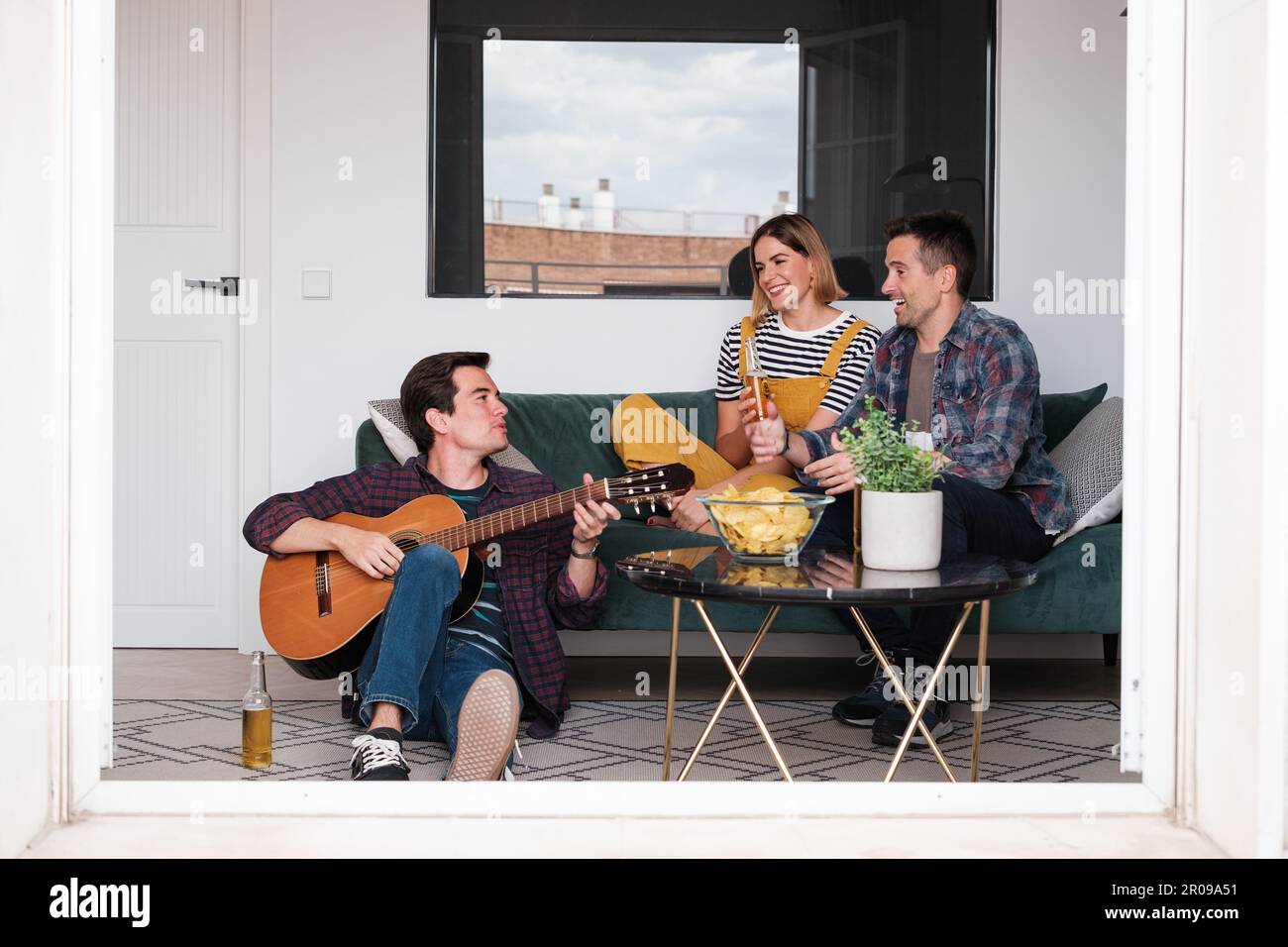 Three friends playing the guitar and having a few beers entertaining at ...