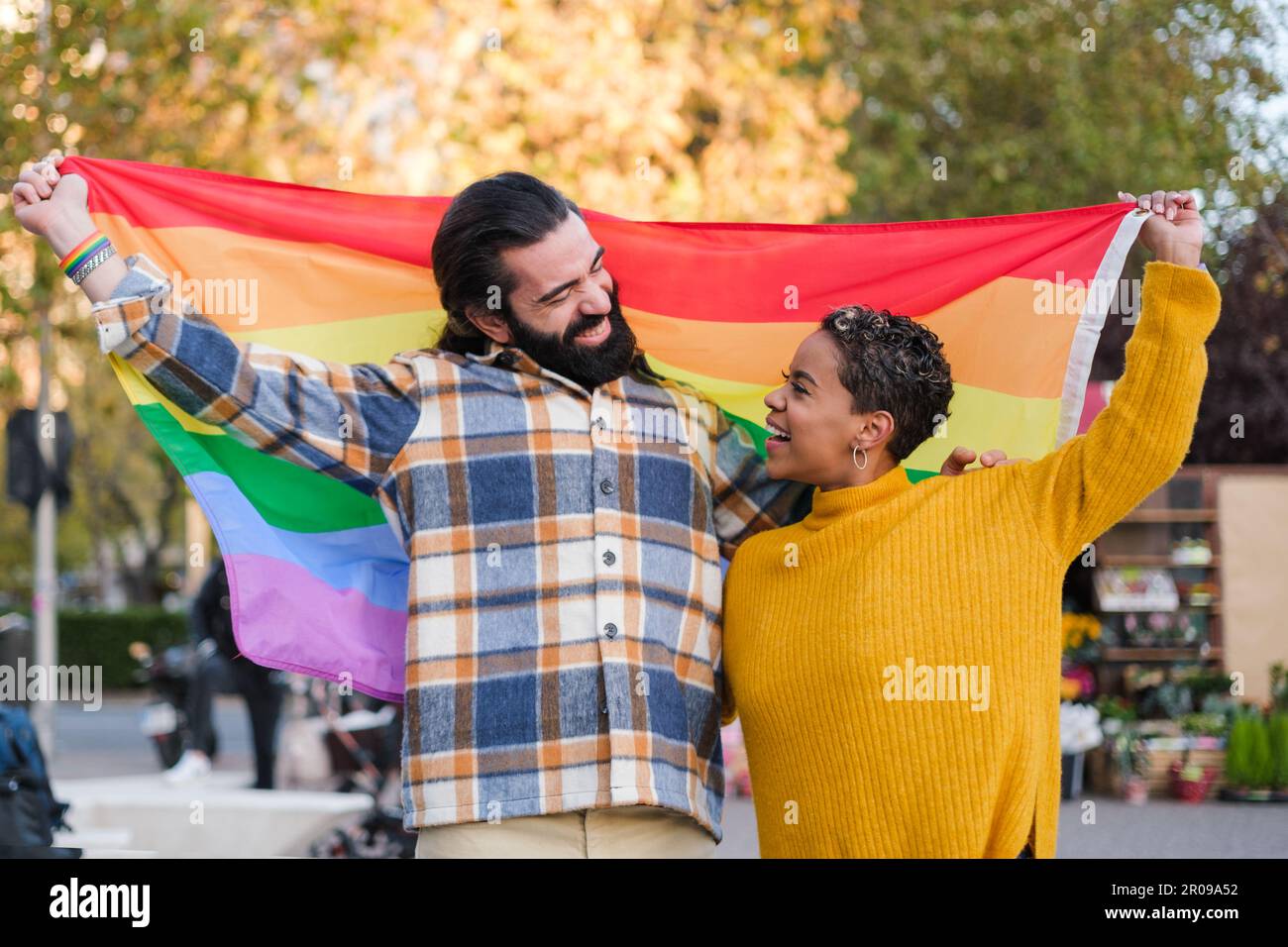 Young man and woman holding lgtbi pride flag and smiling outdoors ...
