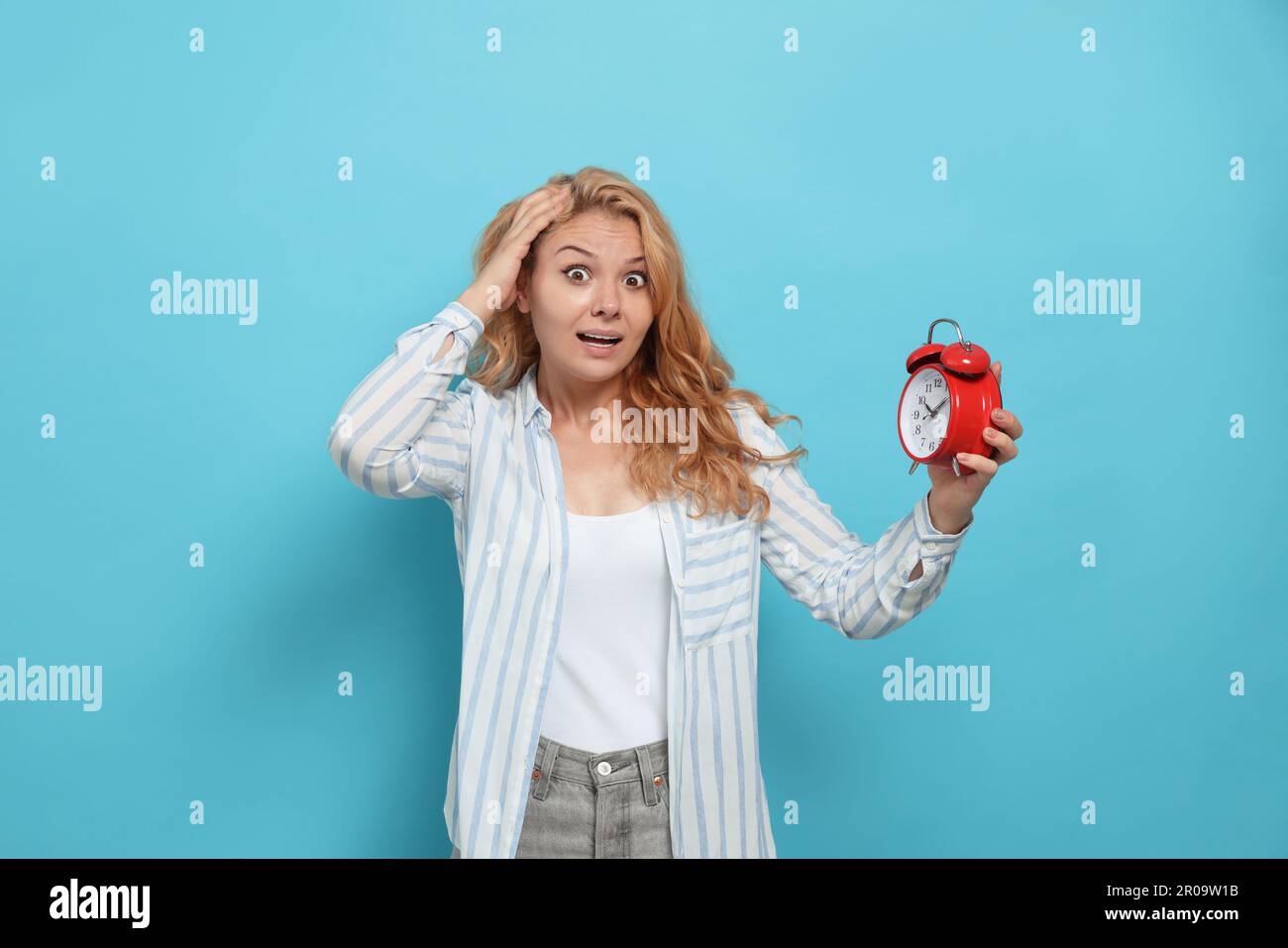 Emotional woman with alarm clock in turmoil over being late on light ...