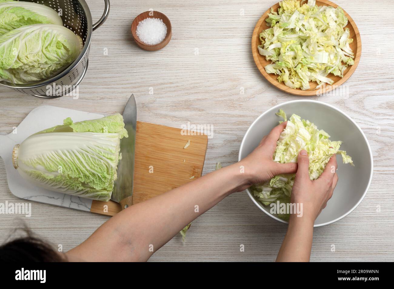 Woman putting cut Chinese cabbage into bowl at white wooden kitchen ...