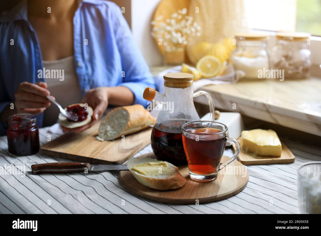 Woman spreading jam onto bread at table indoors, focus on aromatic tea ...