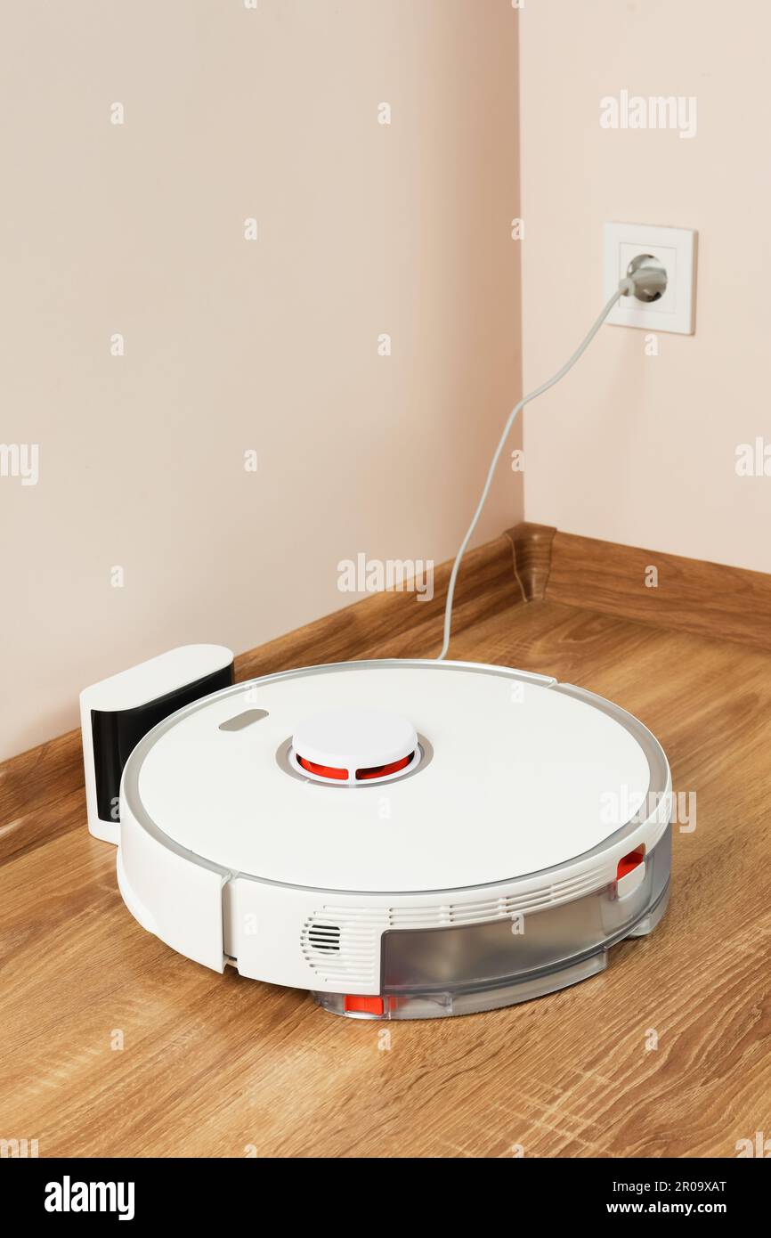 Robotic vacuum cleaner charging on wooden floor indoors Stock Photo - Alamy