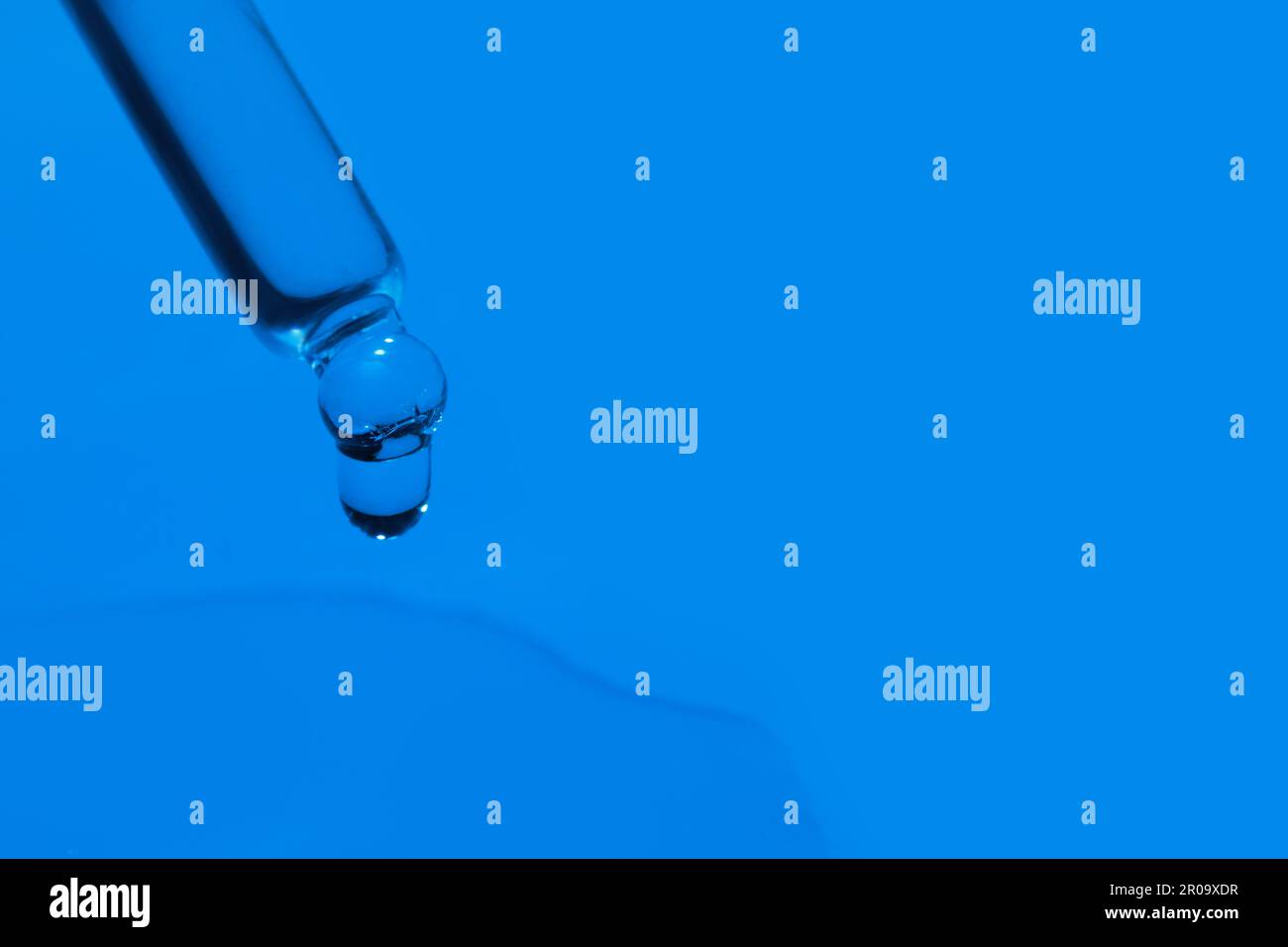 Dripping face serum from pipette on blue background, closeup. Space for ...