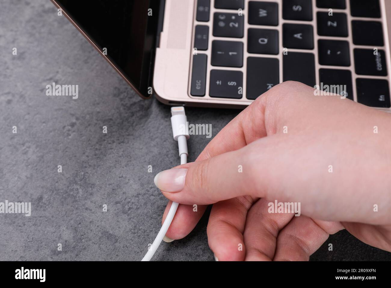 Woman plugging USB cable with lightning connector into laptop port on ...