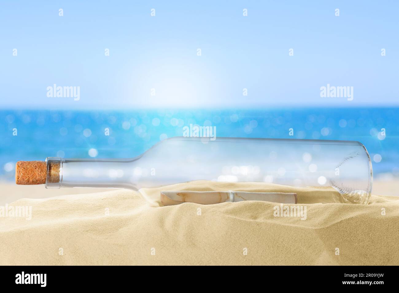 Corked glass bottle with rolled paper note on sandy beach near ocean ...